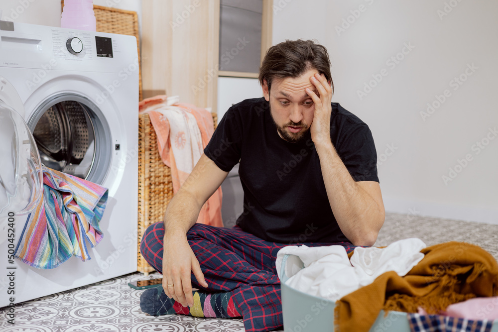 Guy sits on the laundry room floor with the washing machine open ...