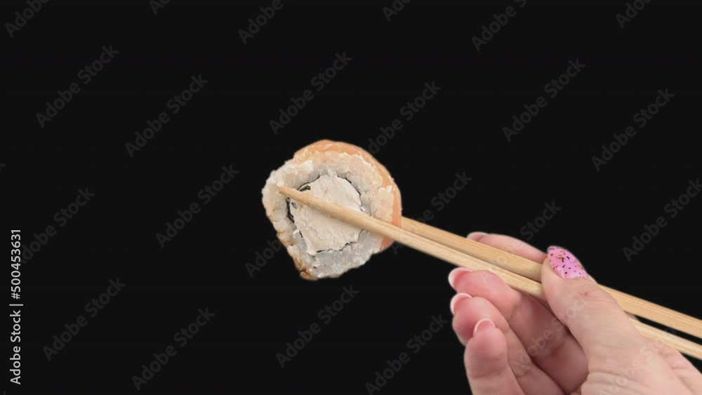 Female hands hold Japanese chopsticks with sushi rolls on transparent background. Alpha channel ...