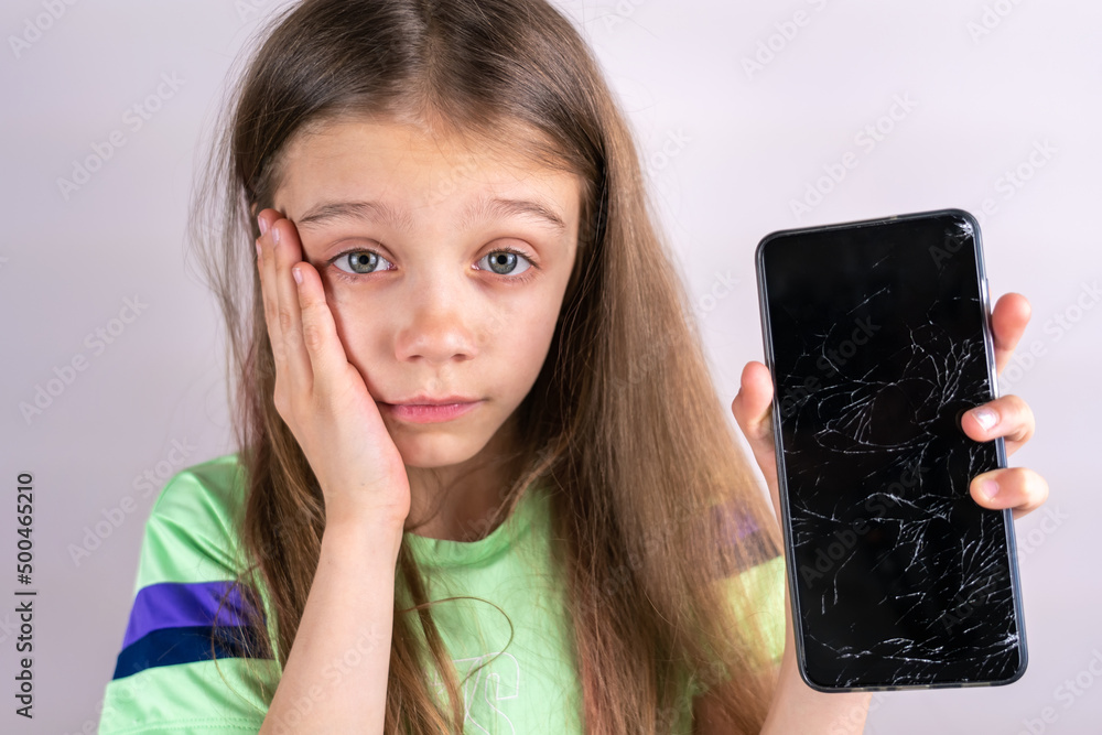Portrait of terrified child with damaged phone. Upset little girl ...