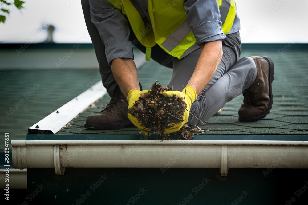 Fotografia do Stock: A man worker is cleaning a clogged roof gutter ...