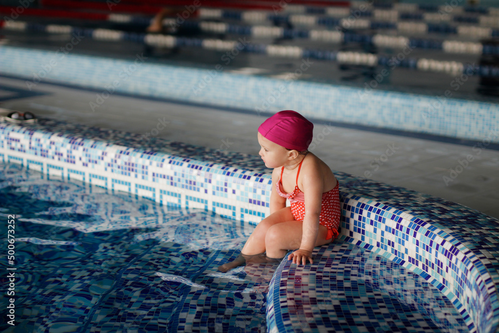 Cute child toddler in cap and swimsuit sits on edge of pool, Kid is ...