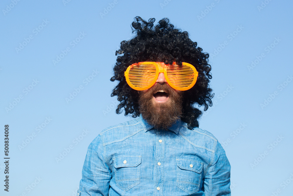 Crazy funny bearded man with wig and fun glasses on sky background ...
