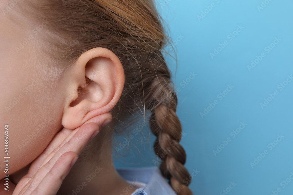 Cute little girl showing hand to ear gesture on light blue background ...