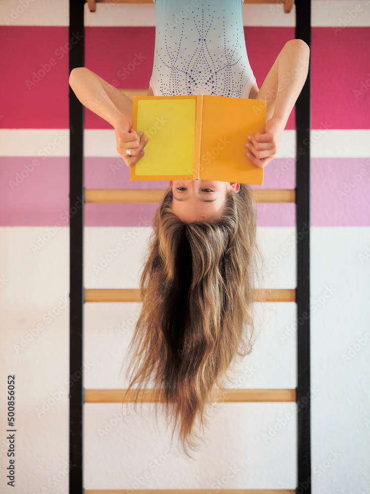 Girl reading book hanging upside down on wall bars Stock Photo | Adobe ...