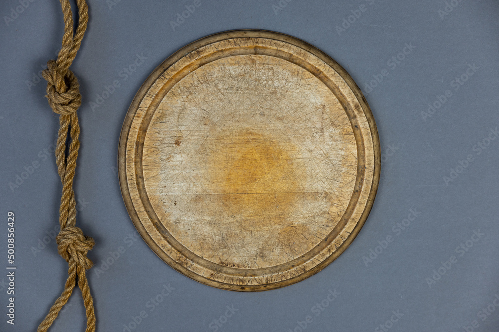 Round wooden cutting board and ship's rope against the gray background ...