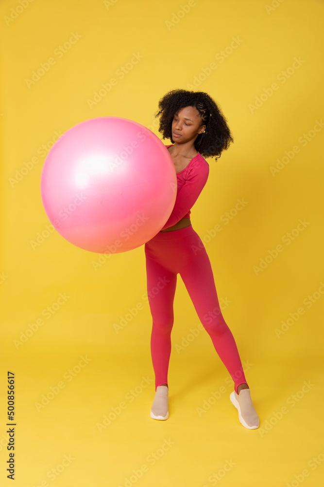 Young woman holding pink balloon standing against yellow background ...