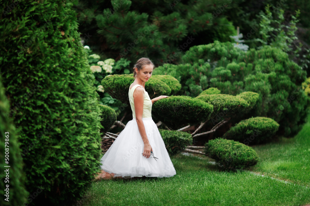 Beautiful woman girl in a dress with garden scissors cuts juniper ...