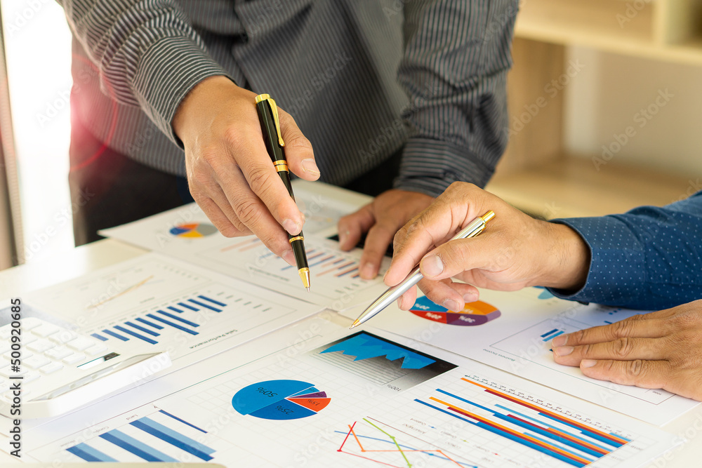 2 businessmen with pens pointing to financial charts for analysis ...