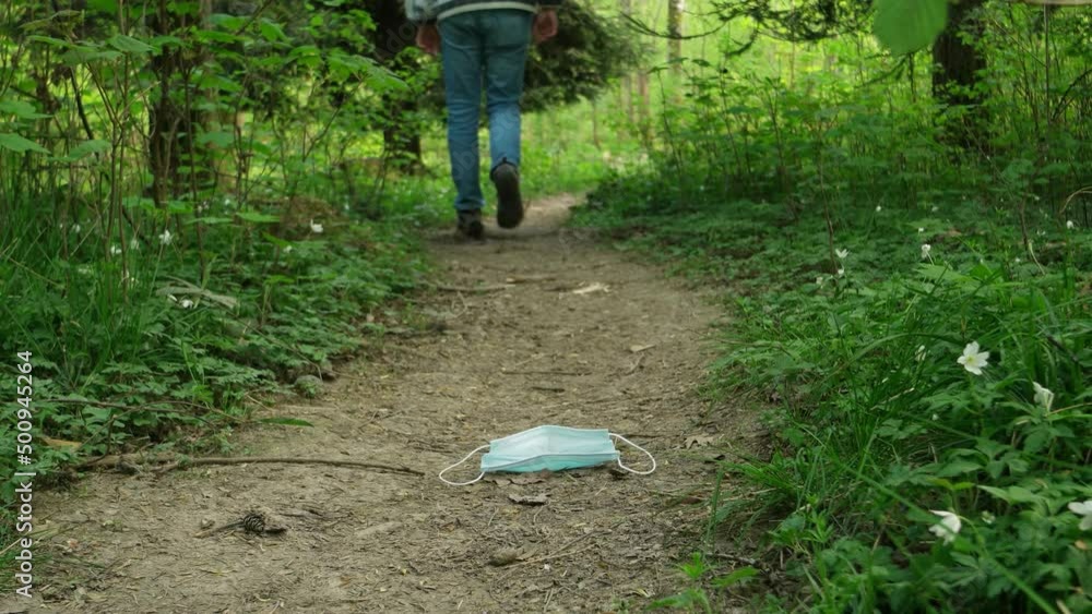 Caucasian male dropping a medical face mask and littering on a footpath ...