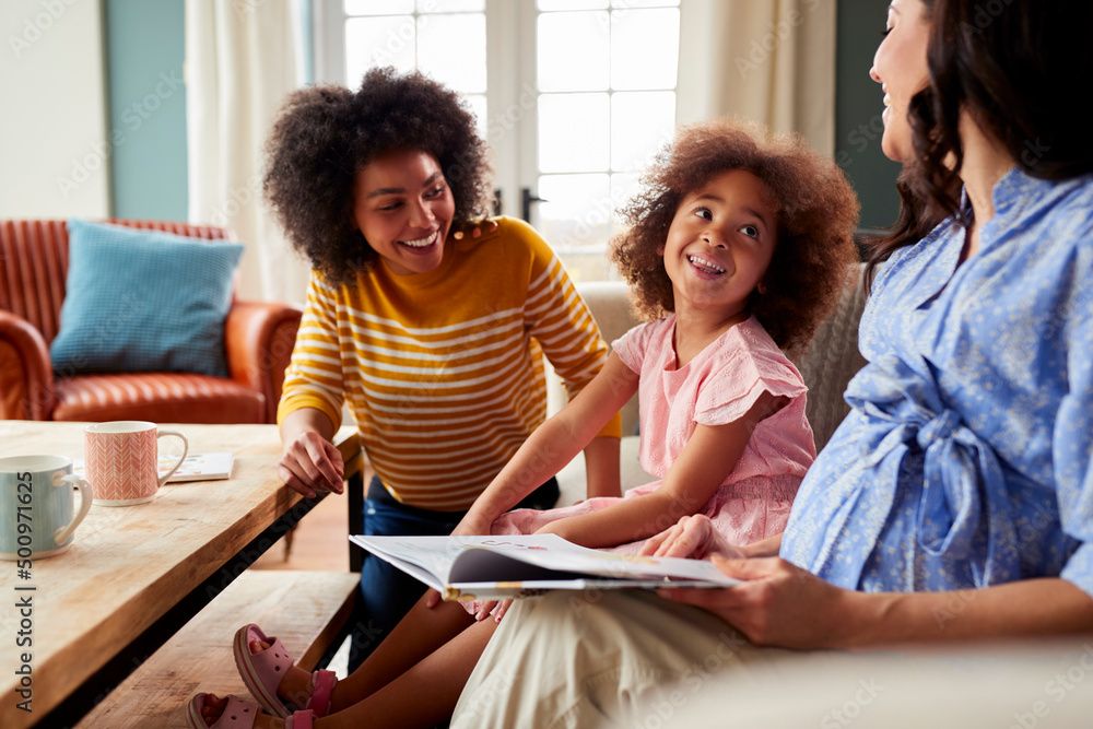 Family With Two Mums Wearing Pyjamas Reading Story Book At Home With ...
