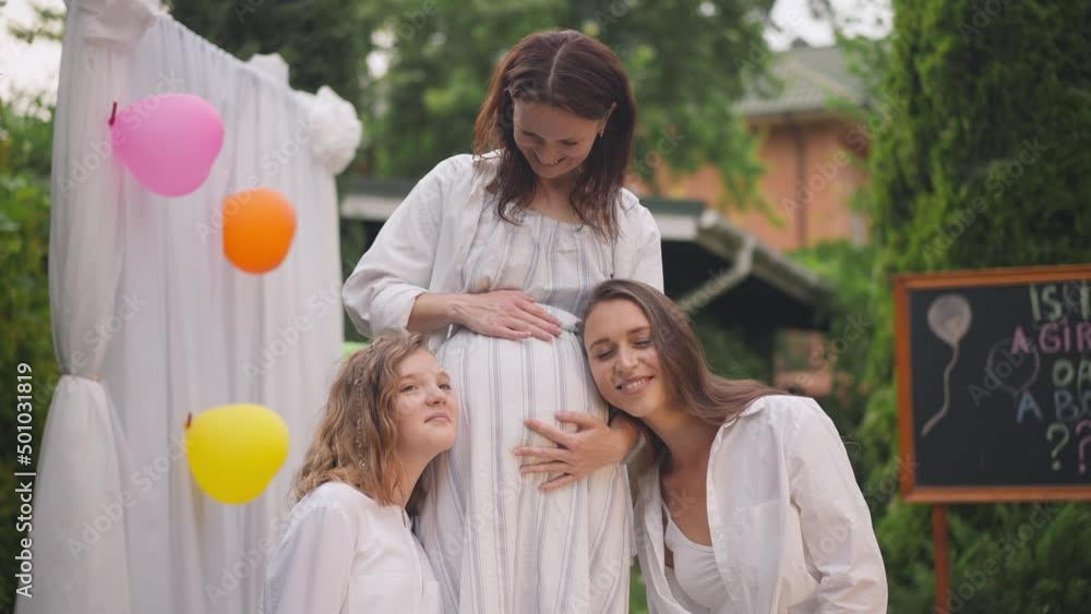 Smiling pregnant woman standing on backyard as friends listening to ...