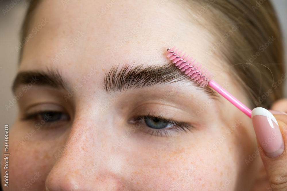 The master combs the eyebrows of the client after lamination of the ...