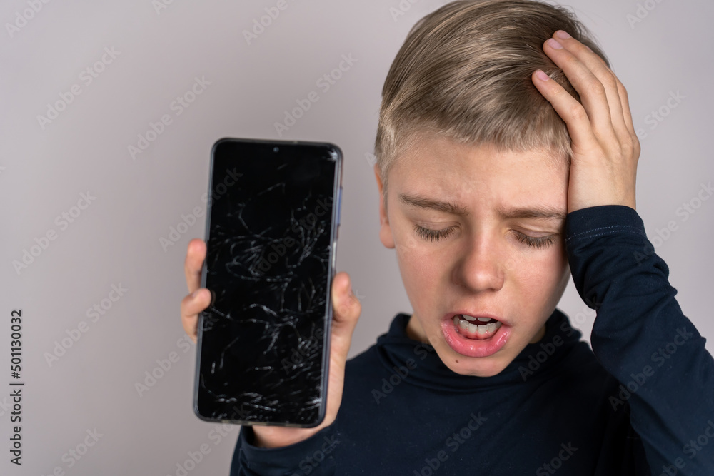 Scared teen boy with emotional expression showing broken smartphone ...
