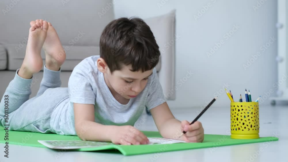 School boy lying on floor and drawing with pencil. cute kid, boy making ...