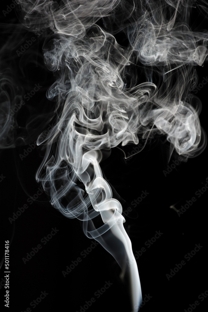 Puffs and curls of white smoke against a black background rising from a ...