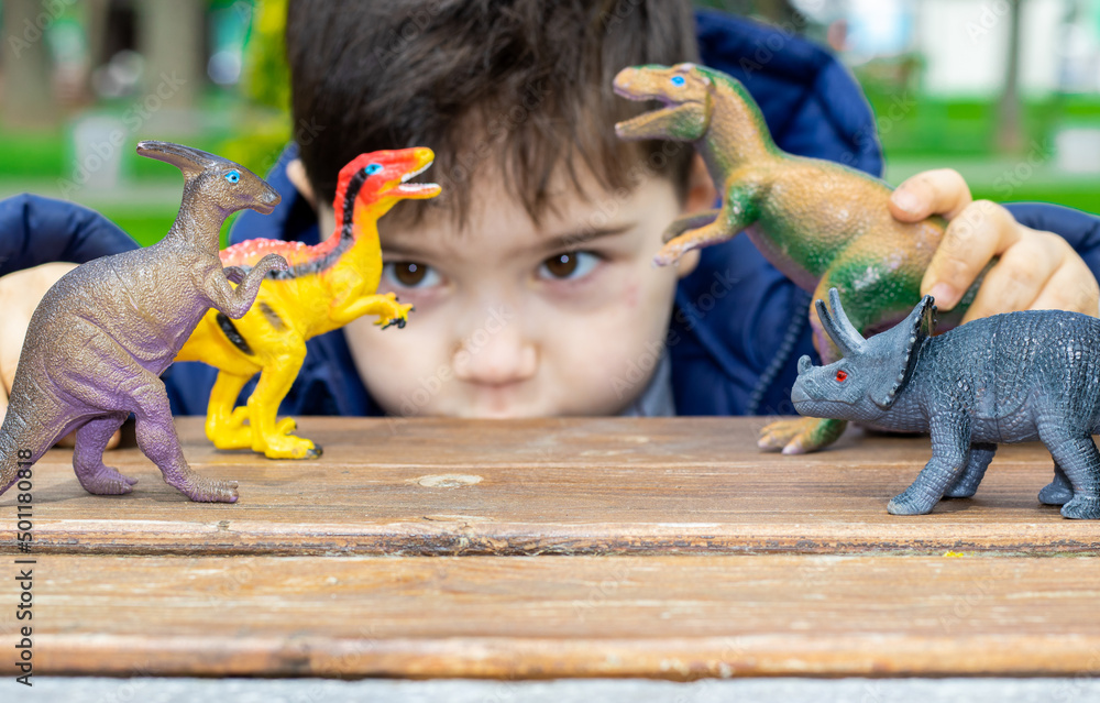 cute kid is playing with dinosaurs toys on park bench, spring, green ...