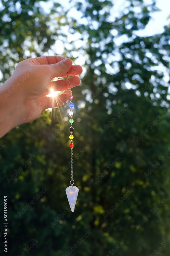 Hand holding dowsing pendant against abstract blurred green natural ...