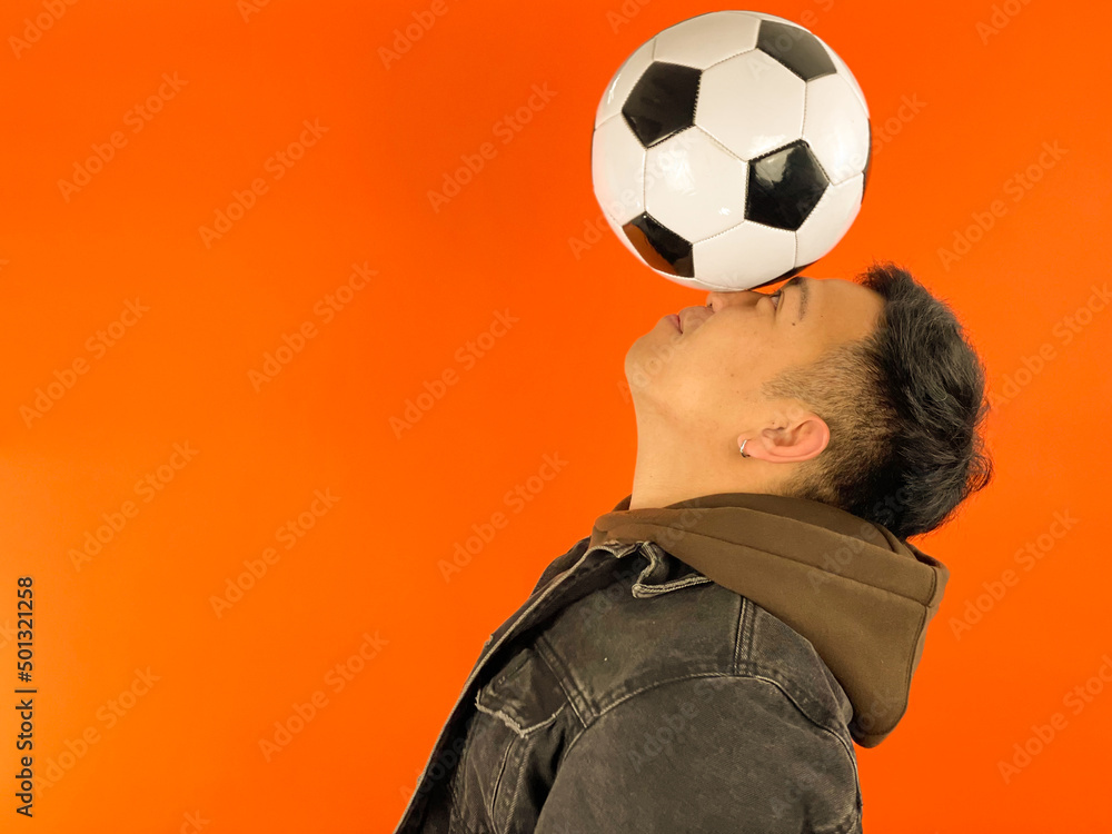 Young Asian man poses with a soccer ball on his head. He wears casual ...