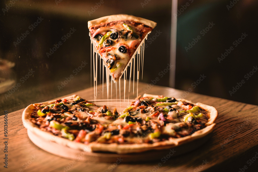 Hot pizza and slice with melting cheese pull on wooden table ...