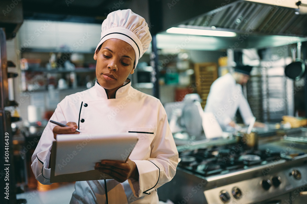Black female chef going through checklist while working in kitchen at ...