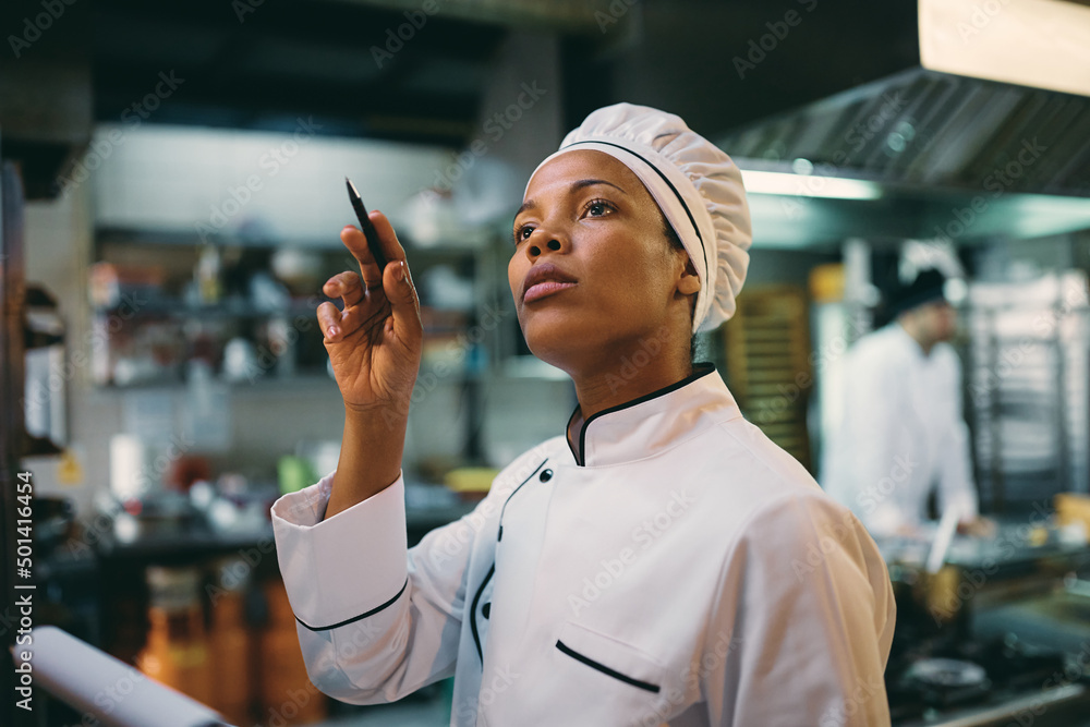 Black female chef examining stock of groceries at restaurant kitchen ...