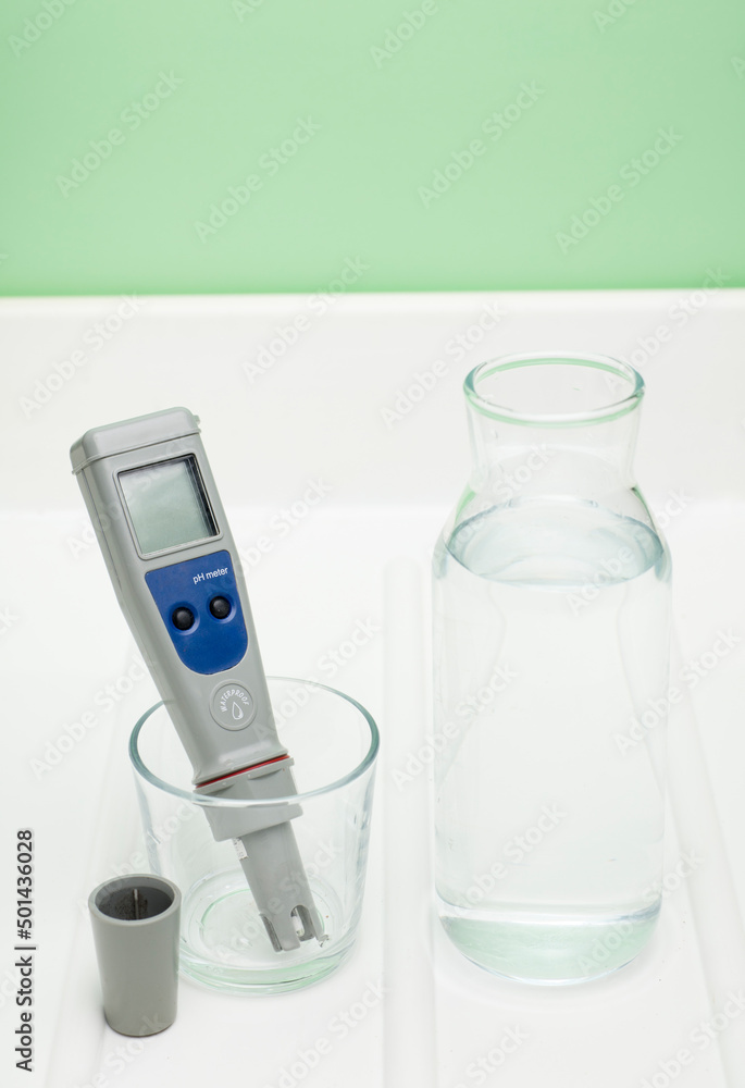 pH meter in a glass of water, and bottle on a white and green ...