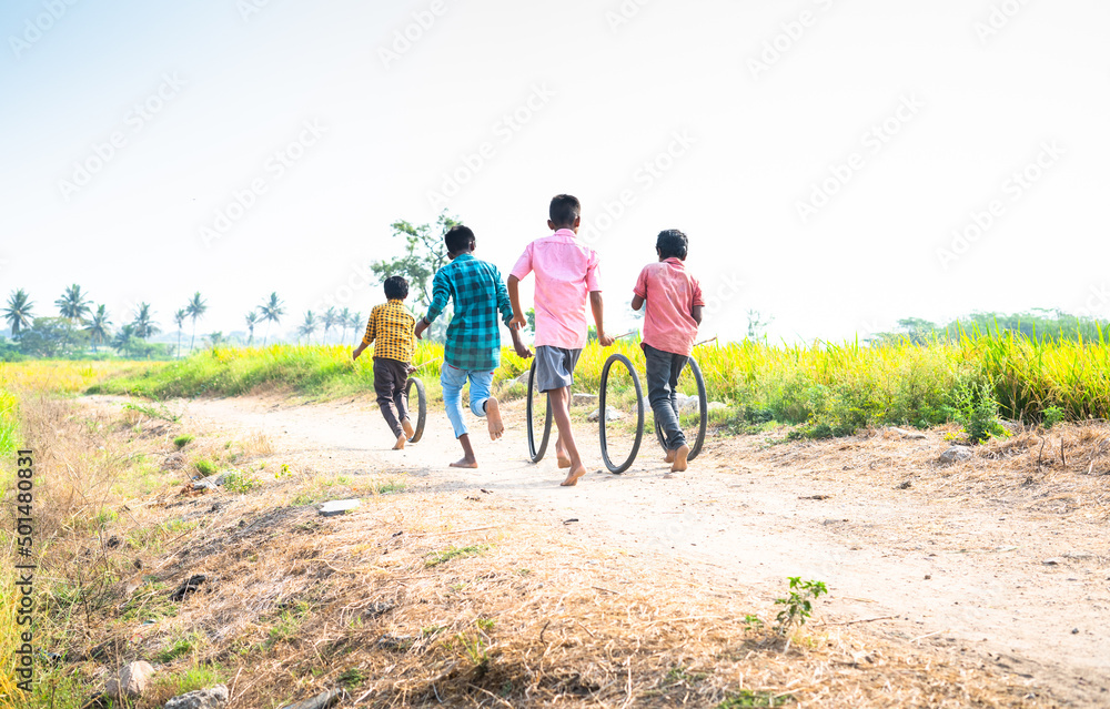 back view shot of Indian village kids playing with tyre wheel by ...