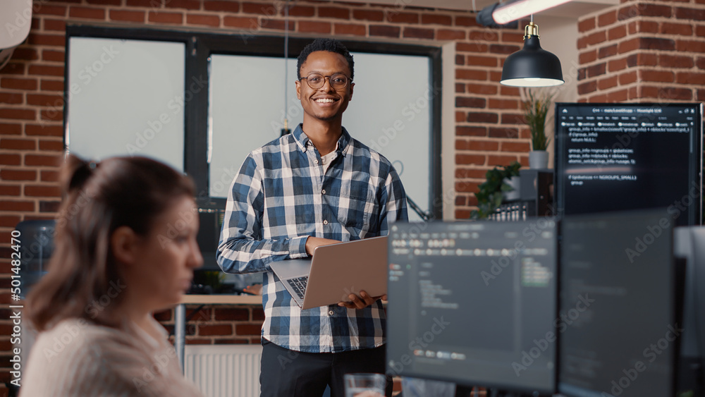 Portrait of african american software developer holding laptop looking up and smiling at camera ...