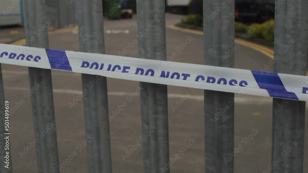 Close up as police detective cordons off an industrical unit by pacing ...