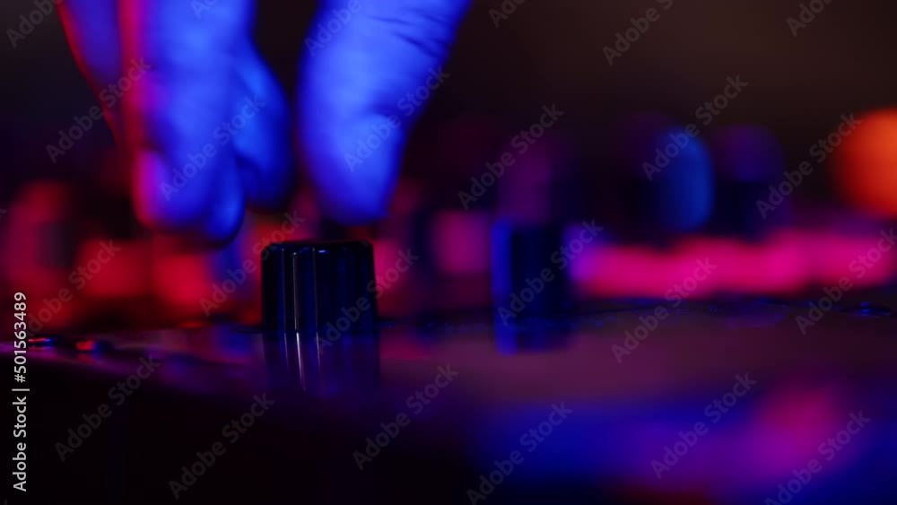 Closeup of DJs hands twisting knobs on mixing console adjusting volume of music in nightclub ...