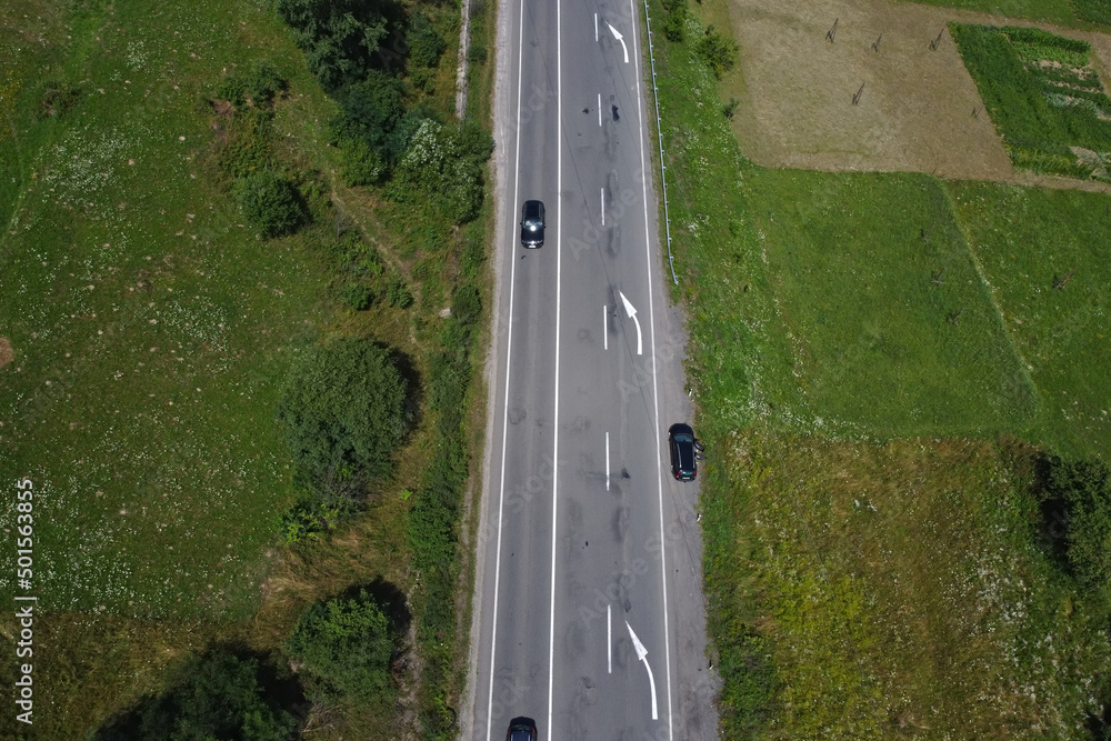 Aerial view from drone of highway with three lanes between green fields ...