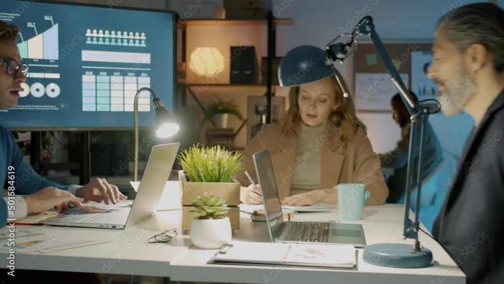 Group of employees working in dark office using laptops and talking in ...