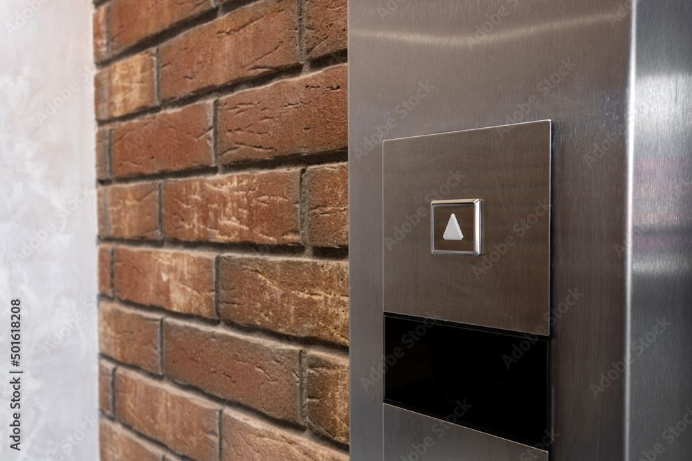Button to call the elevator up on a metal panel with a red brick wall ...