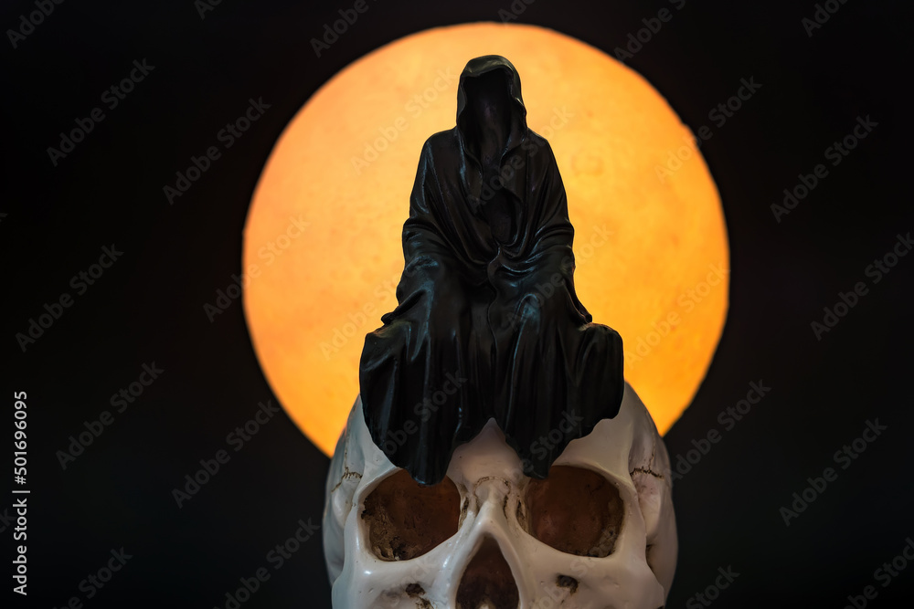 A statue of a grim reaper sitting on a skull on a full moon background ...