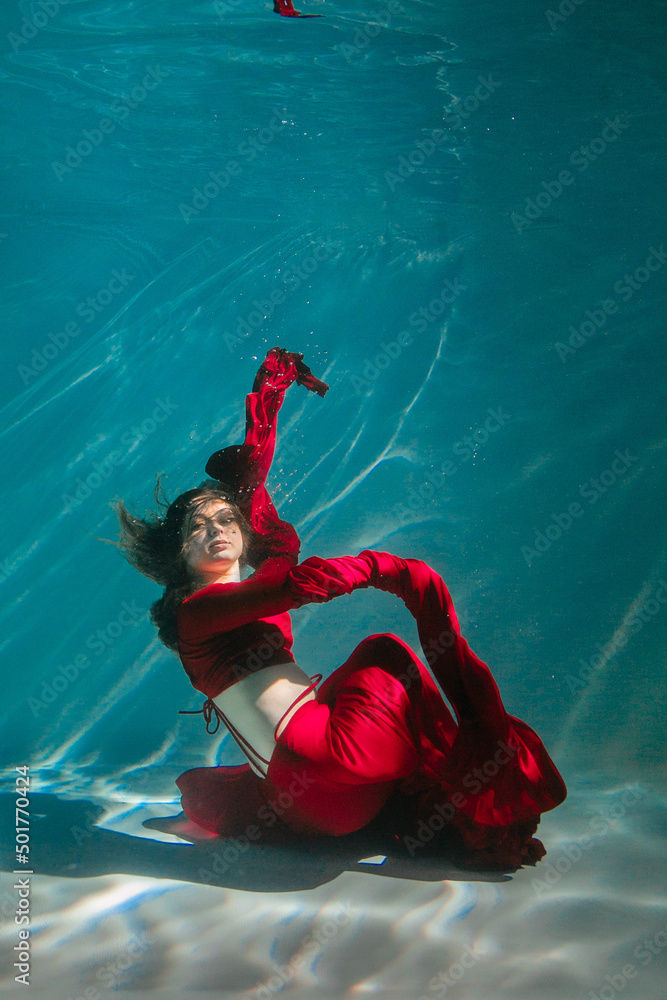 Attractive red-haired young woman swims beautifully underwater in a red ...