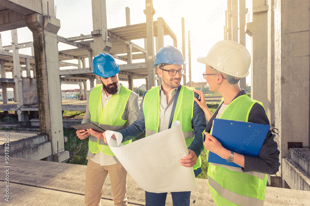 Happy mixed group of young architects looking at building blueprints ...