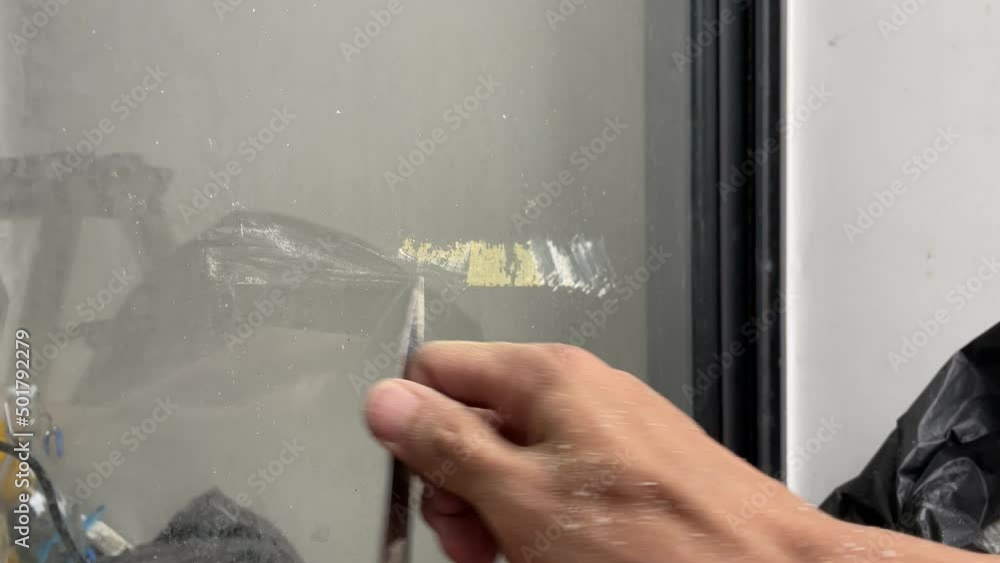 Hand with knife scraping off dry glue sticky on sliding door glass of ...