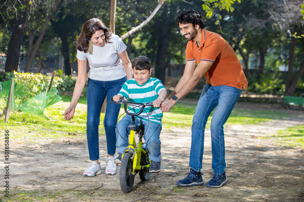 Indian mother and father helping son learn to ride a bicycle in the ...