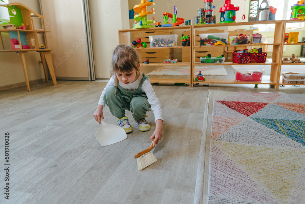 Little girl sweeping the floor using a dustpan and a broom at ...