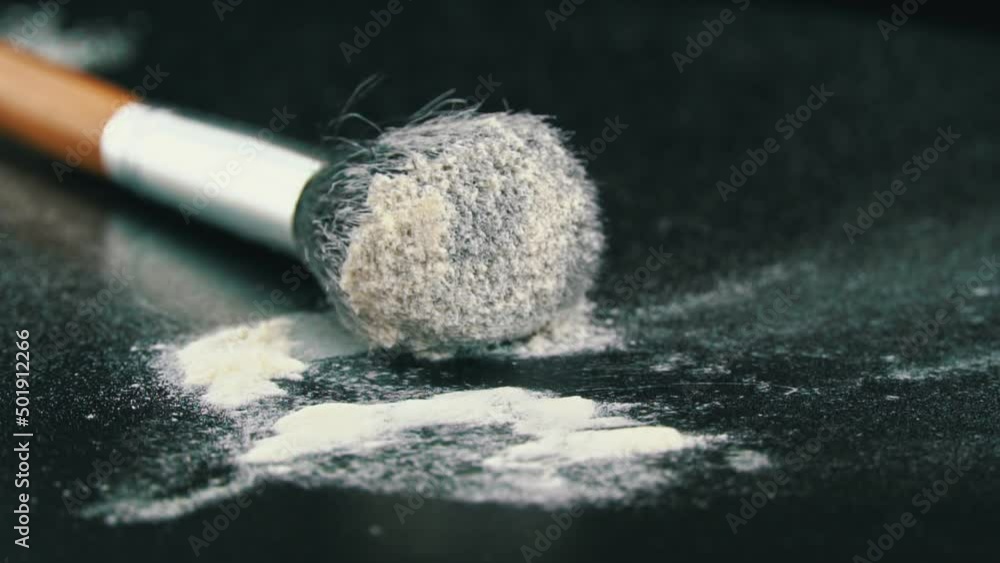 Cosmetic powder for the face is poured from a brush on a black ...