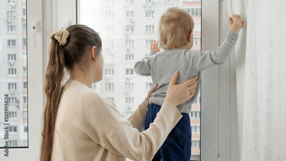 Little baby boy with mother looking out of the window of high store ...