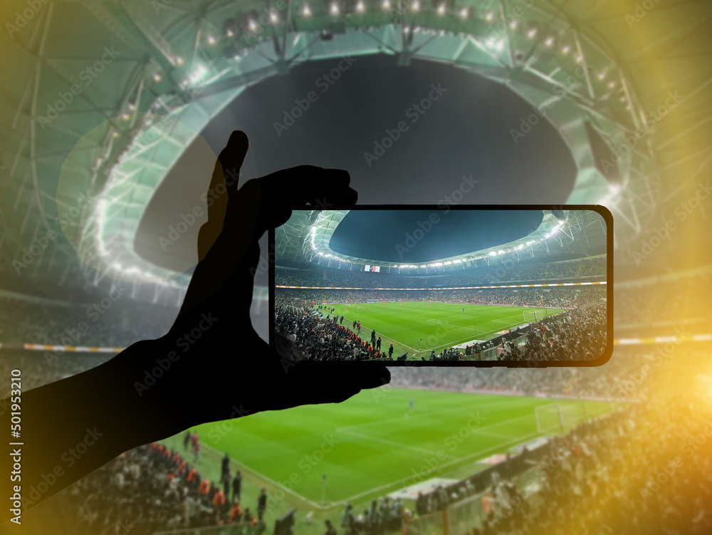 Foto de Fan hand with mobile phone photographing football game. Using a ...