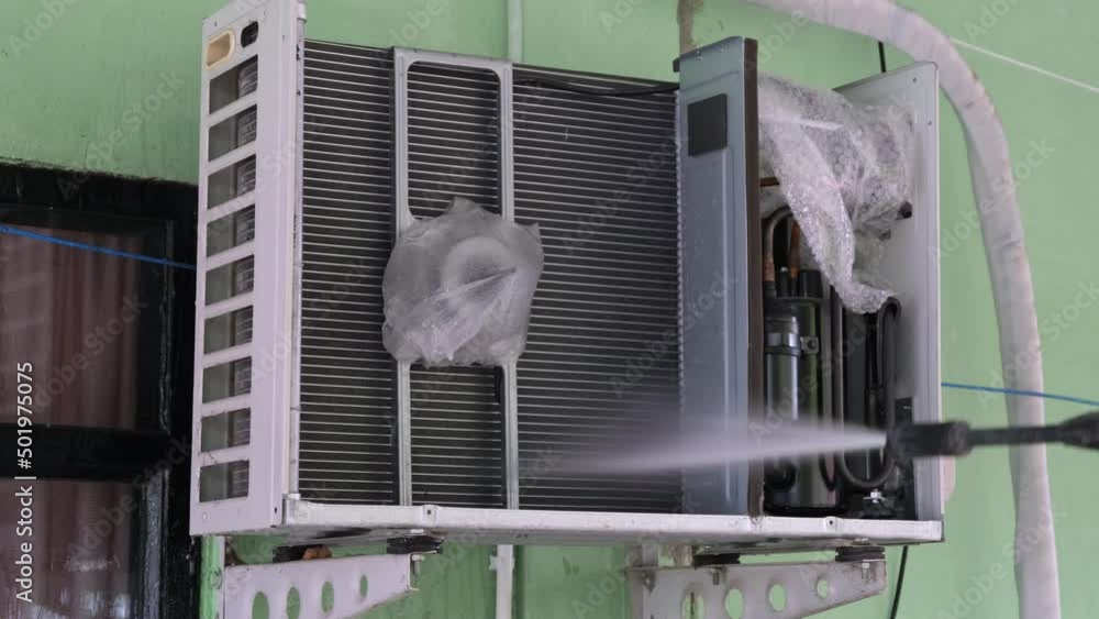 Worker cleaning the air conditioner compressor by spraying water for ...