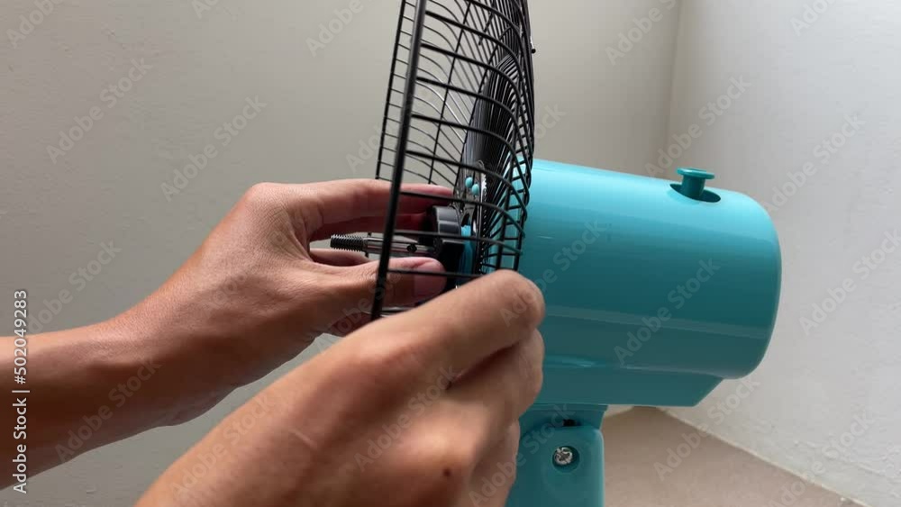 Tighten black plastic nut at rear grille bar on blue desk electric fan ...
