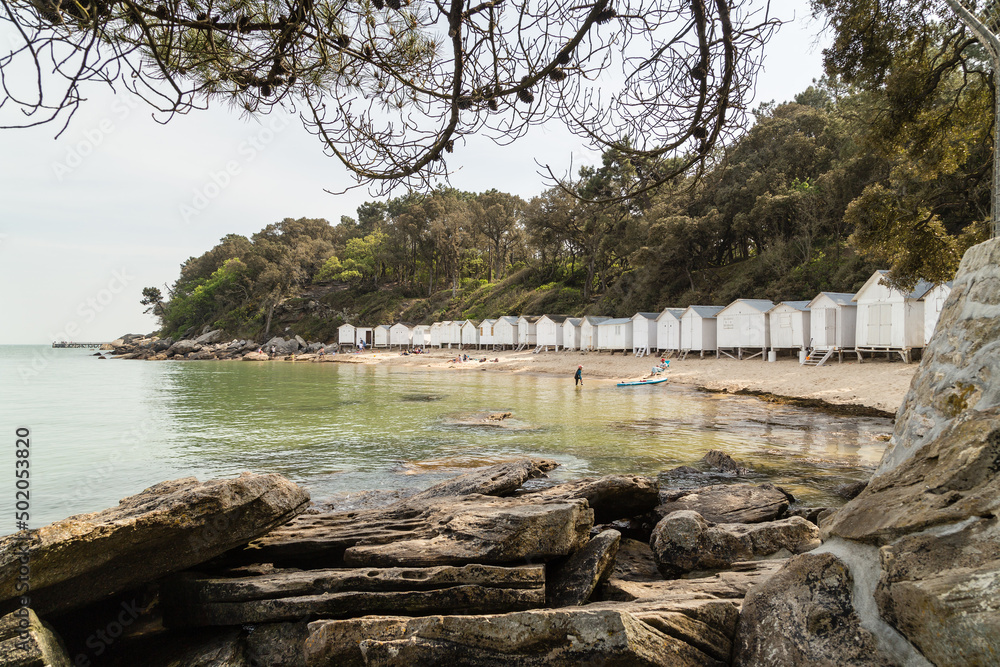 Petite crique avec cabines de plage blanches alignées et dalles de grès ...