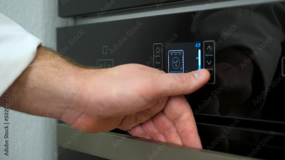 Person hand touching sensor button on electric oven in kitchen. Man ...