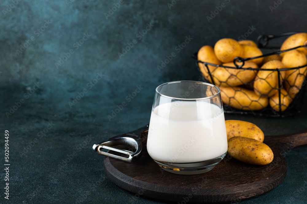 vegan potato milk in glass and potato in bowl on dark background. Vegan ...