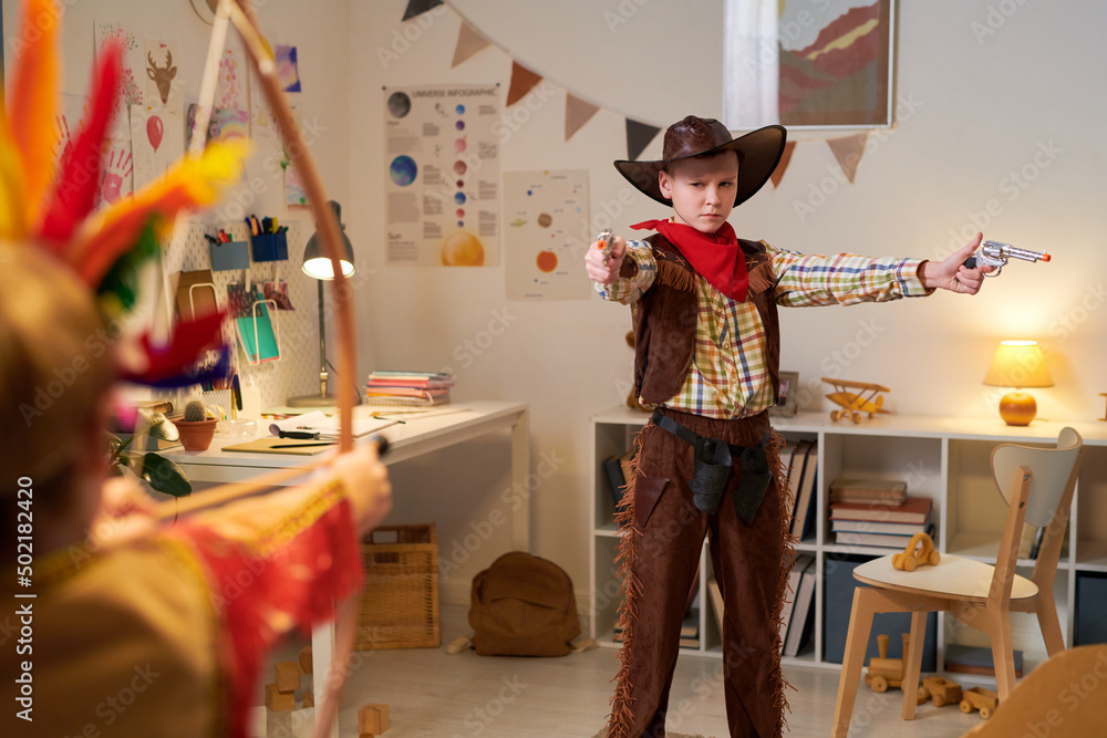 Little schoolboy in costume of cowboy holding two guns during play at ...