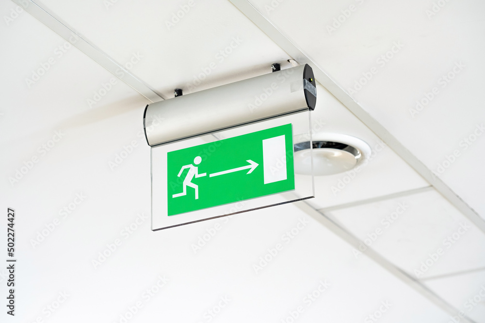 Modern green emergency exit route door arrow sign on the ceiling ...