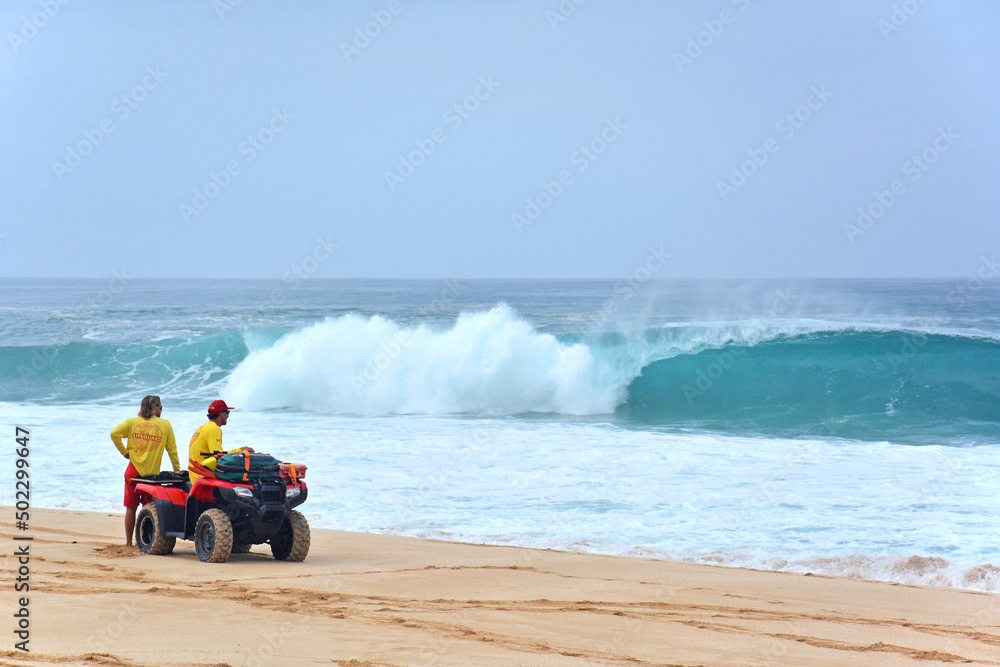Ocean lifeguards patrolling the beach on an ATV under heavy surf ...